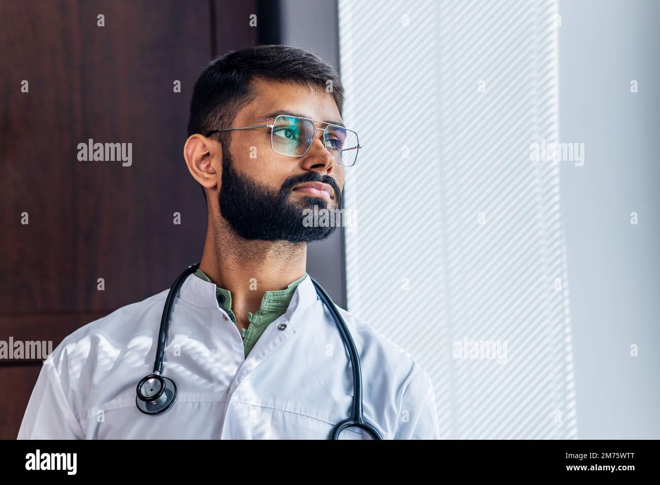 Portrait of male indian doctor wearing white coat in clinic office ...