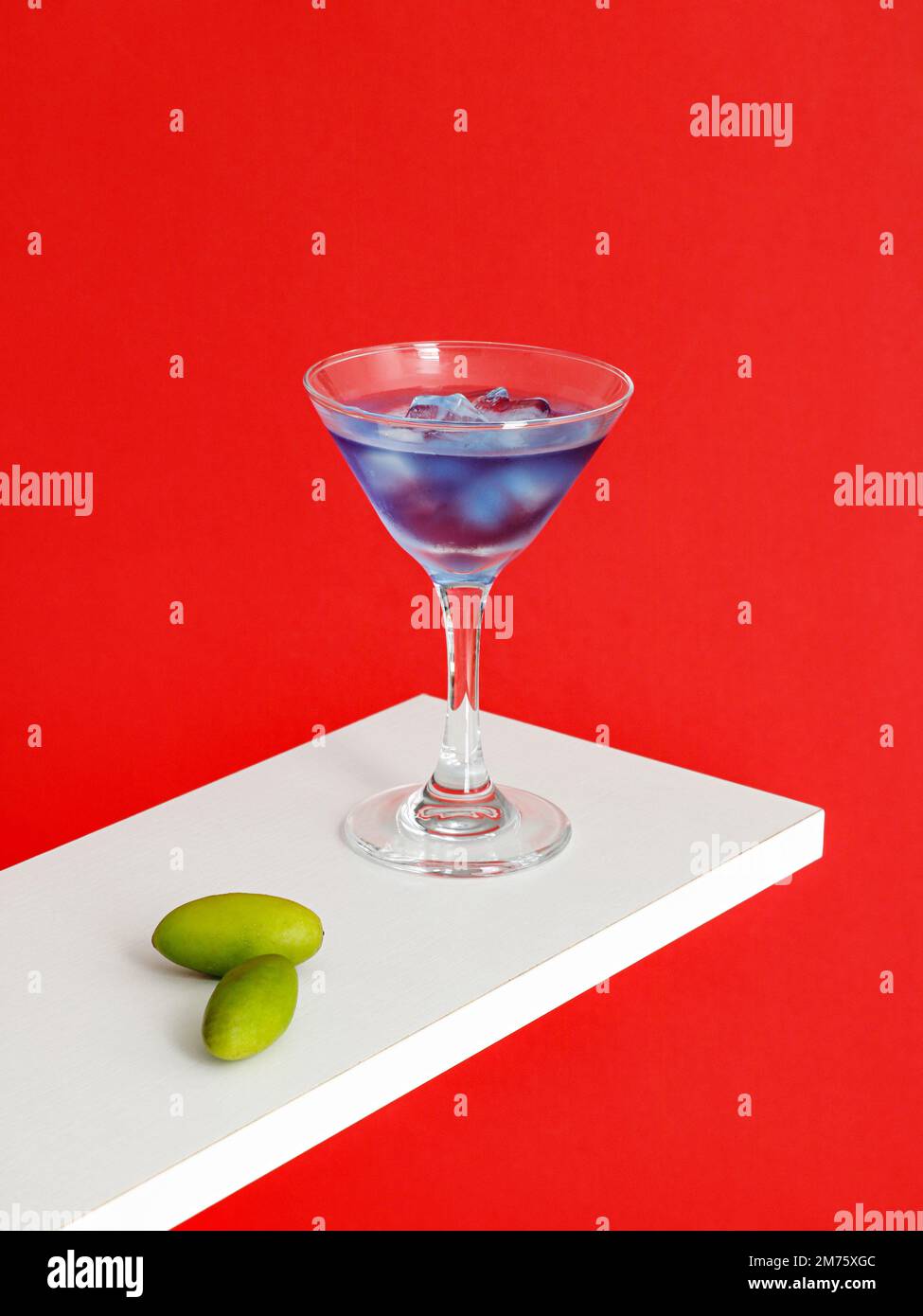 A Blue Moon Cocktail glass and olives on white surface isolated on red ...
