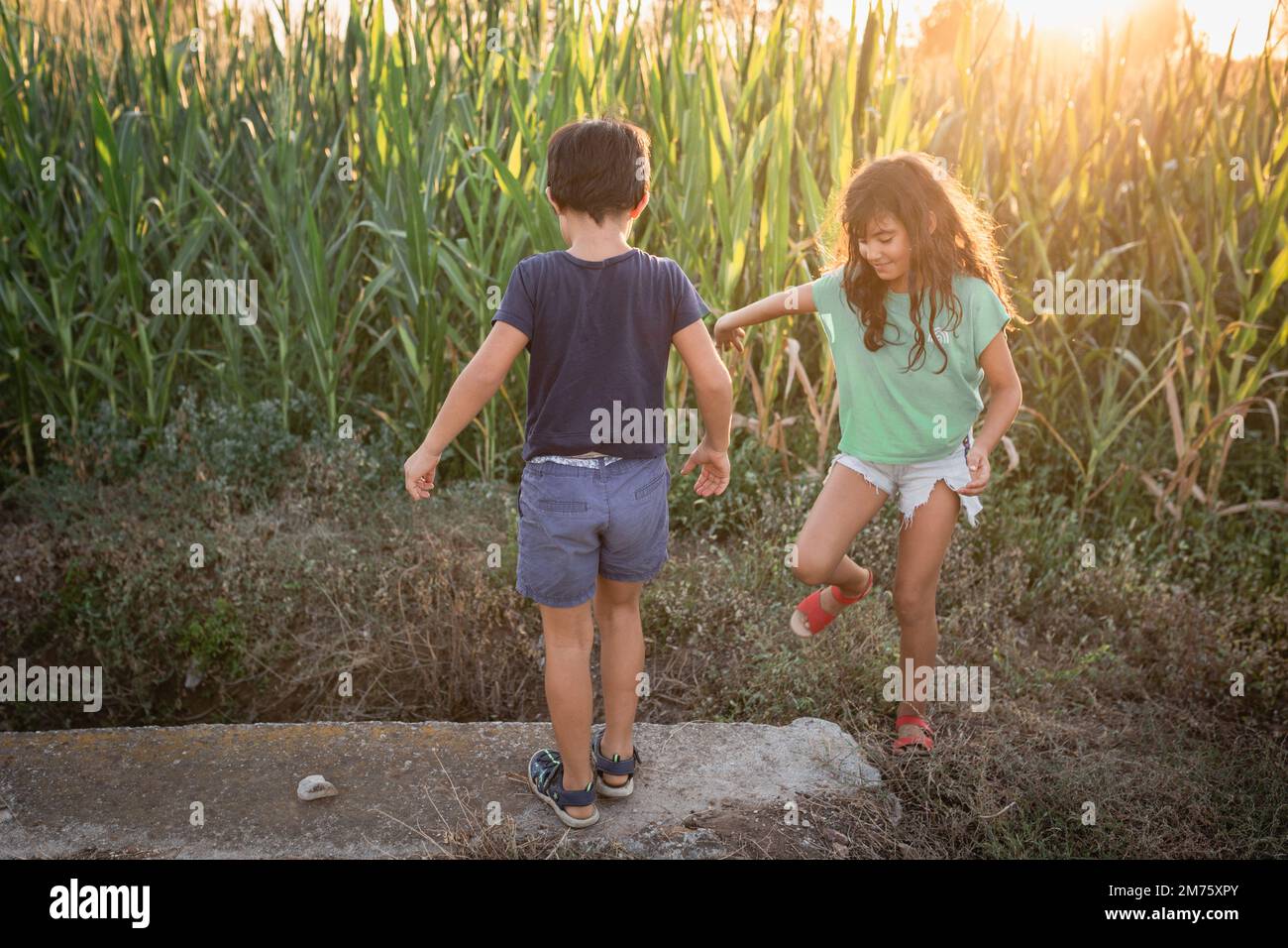 two girls wirh short haircut and long hair jumping over pit in corn ...