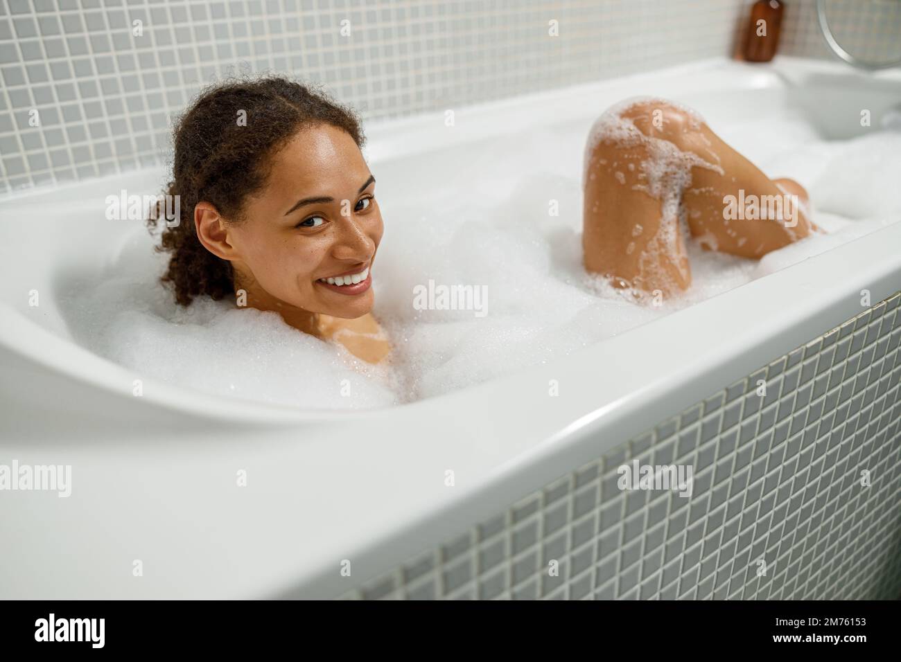 Smiling Afro American Woman Takes Bubble Bath In Bathtub Spa Wellness