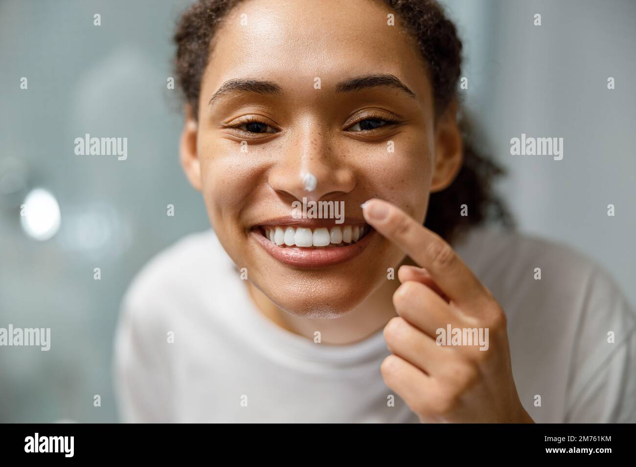 Smiling african woman putting small amount of cream on her nose and ...