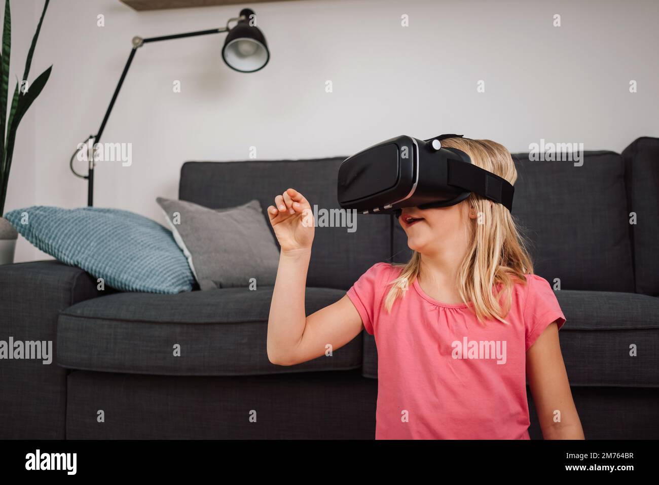 Young girl in VR headset touching air during virtual reality experience ...