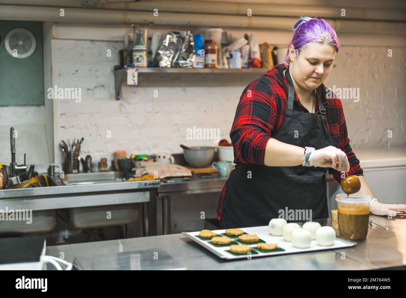 Concentrated female pastry chef in black apron decorating desserts in ...