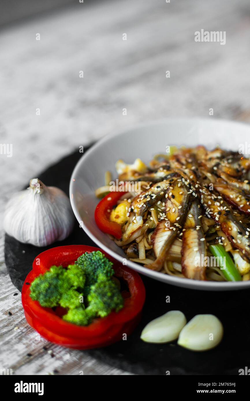 Wok, noodles, udon with eel, on black plate and a wooden white ...