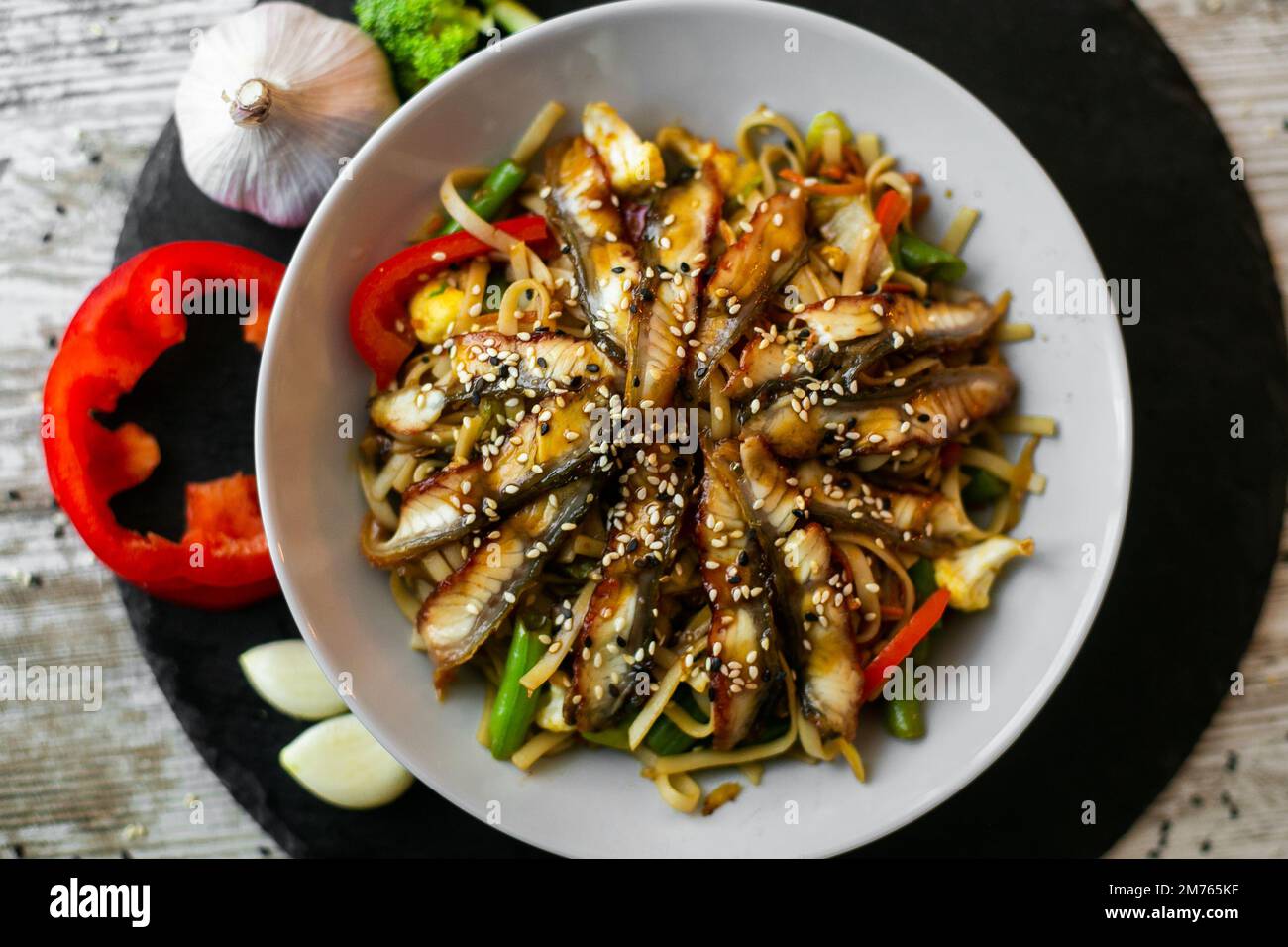 Wok, noodles, udon with eel, on black plate and a wooden white ...
