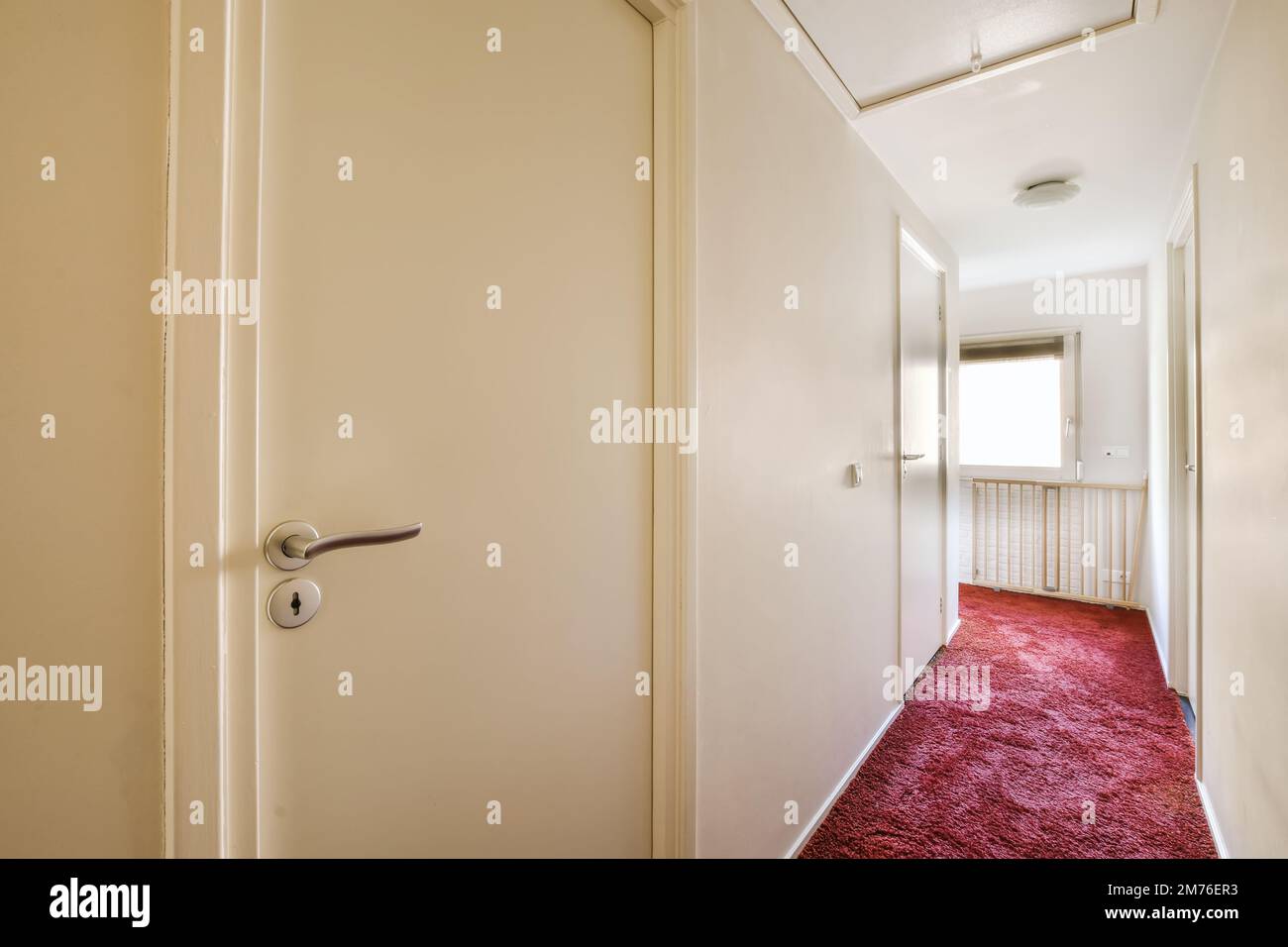 a long hallway with red carpet and white door handle on the left side ...