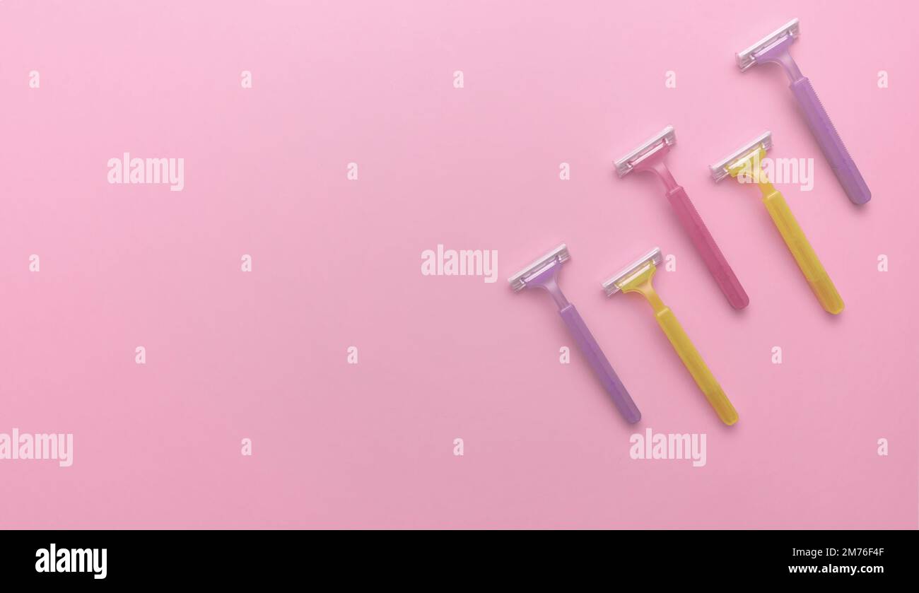 Overhead flat lay of five colorful disposable razors against a pink ...