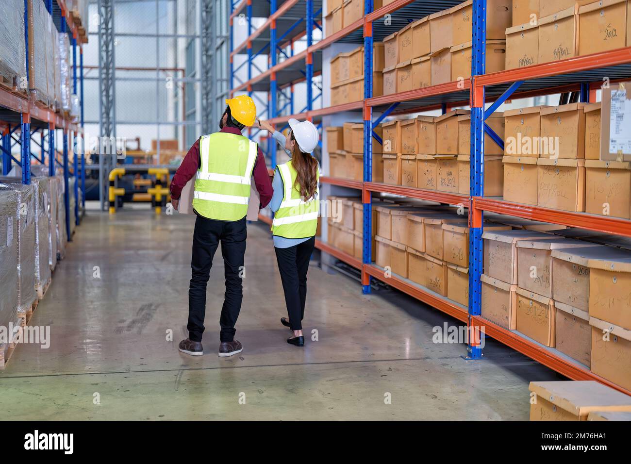 Warehouse worker hold the carton box walk along the steel racking shelf ...