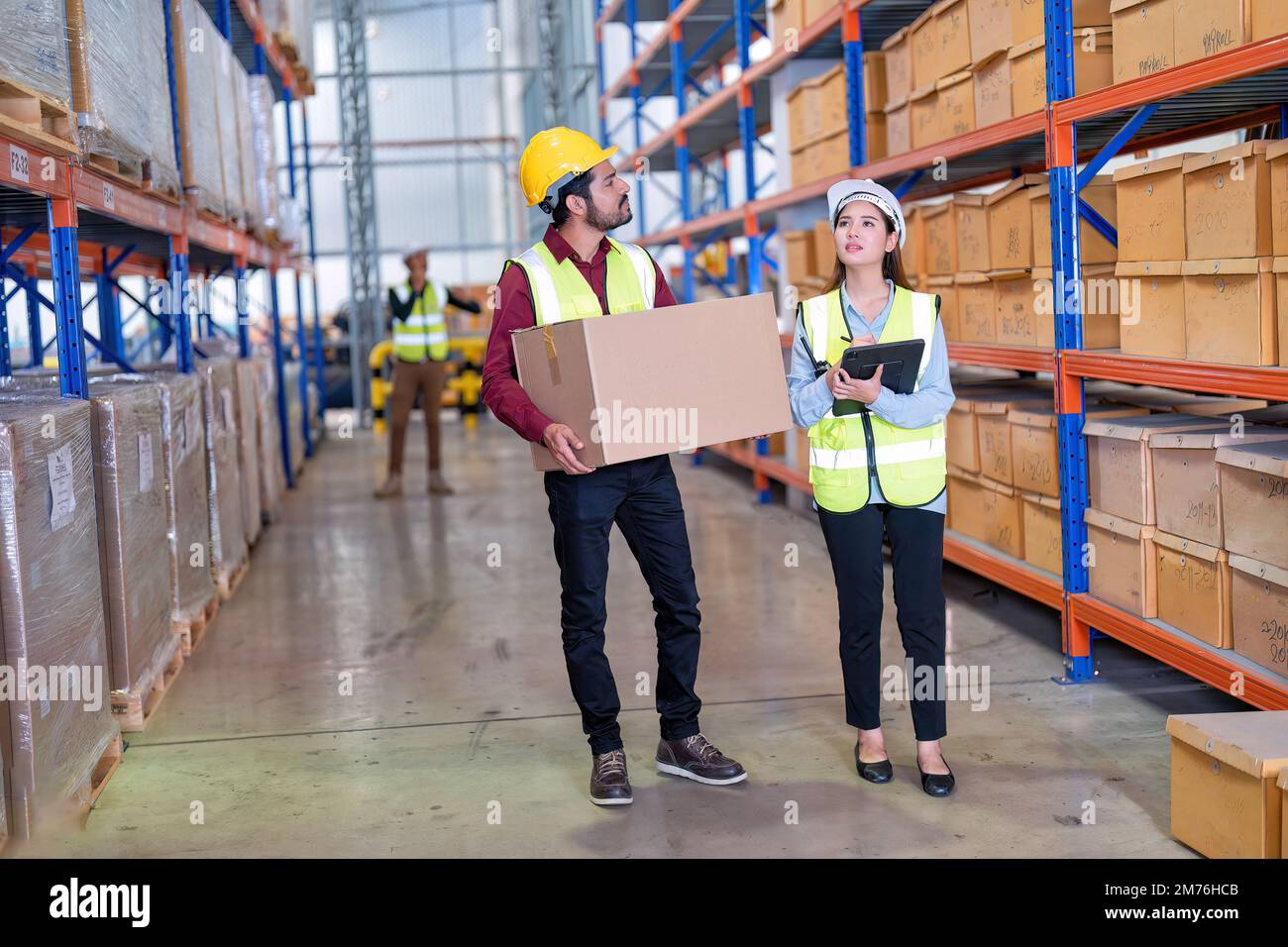 Warehouse worker hold the carton box walk along the steel racking shelf ...