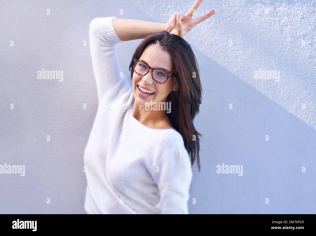 Bunny-eared babe. Portrait of a playful young woman standing against a ...