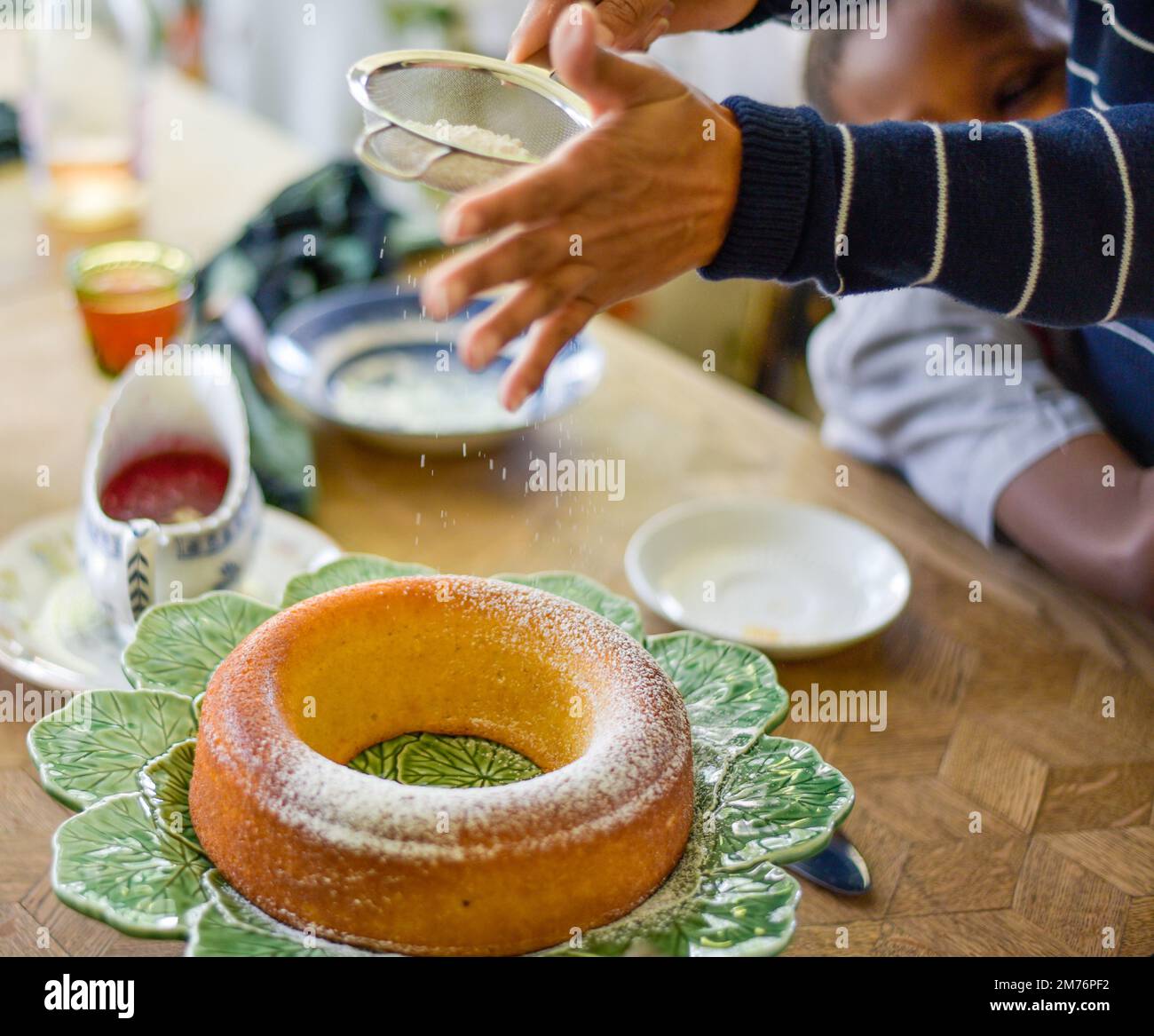 Woman Dusting the top of a moist round sponge cake with fine sifted ...