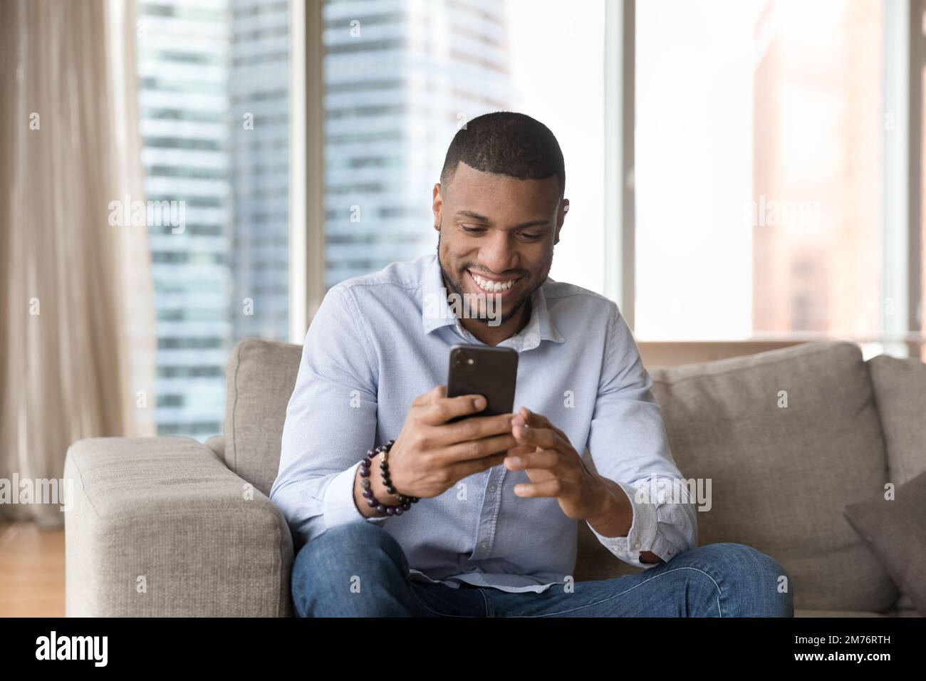 Handsome single African guy sit on sofa with cellphone Stock Photo - Alamy