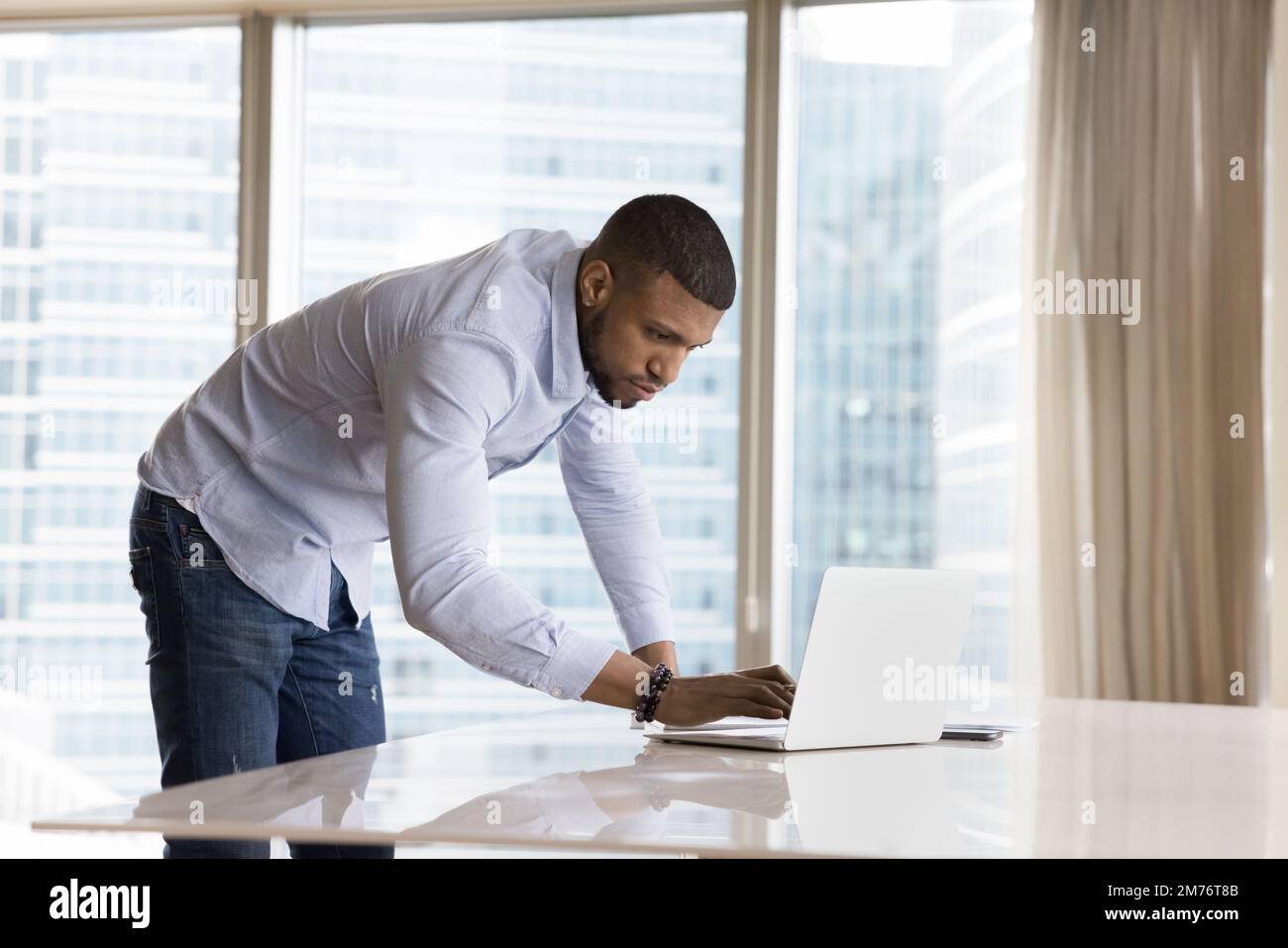 Young African businessman use laptop standing leaned over workplace ...