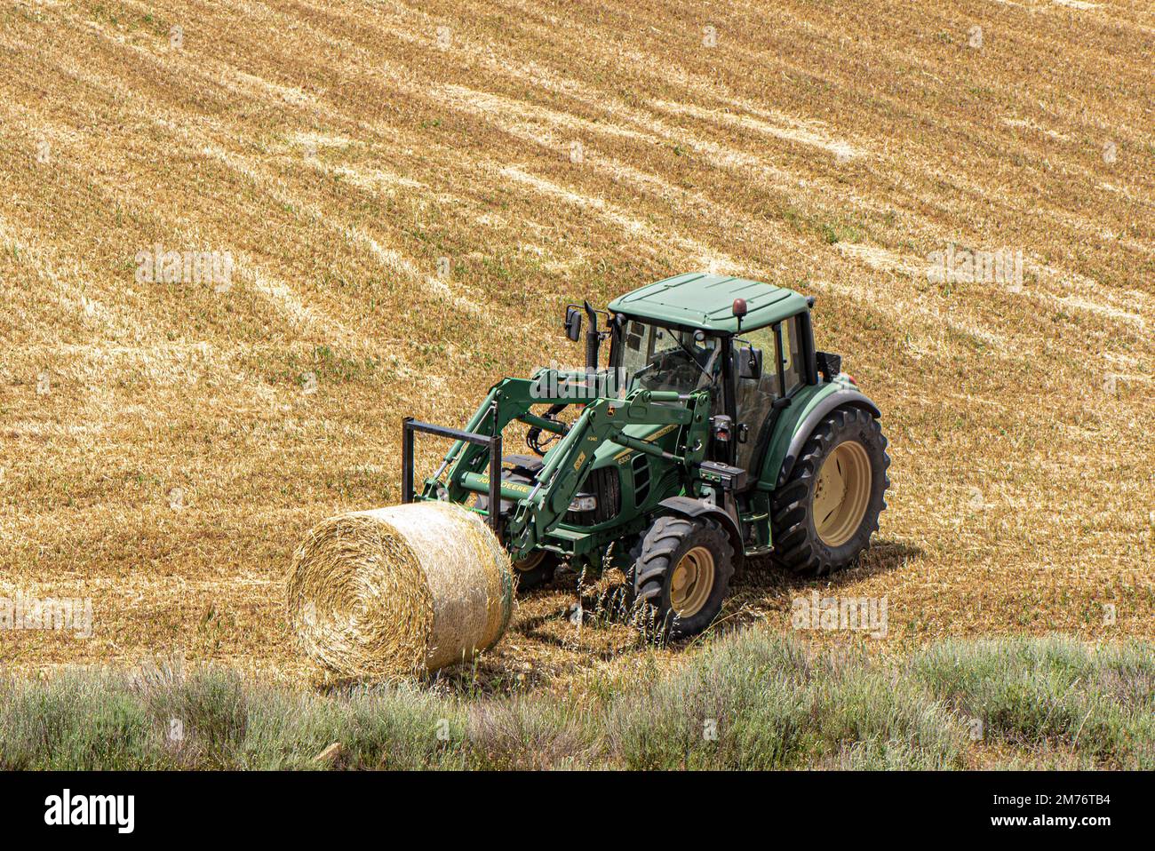 A high angle shot of John Deere tractor lifting a hay bale in an open ...