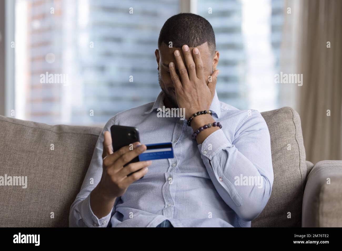 Man holds card and smartphone, feels upset due to scam Stock Photo - Alamy