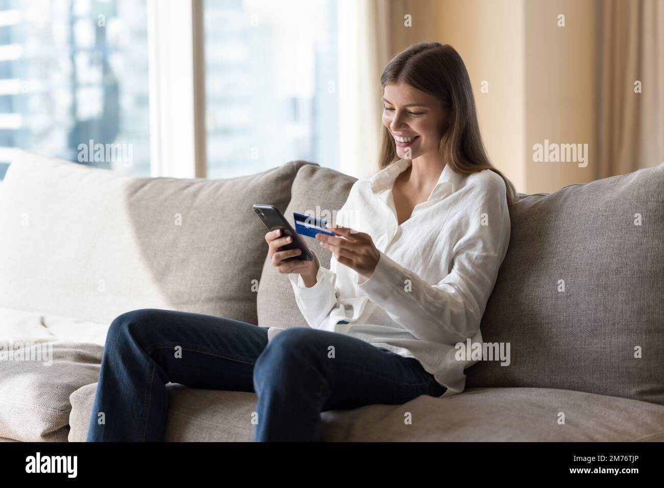 Young woman makes purchase distantly using cellphone and credit card ...