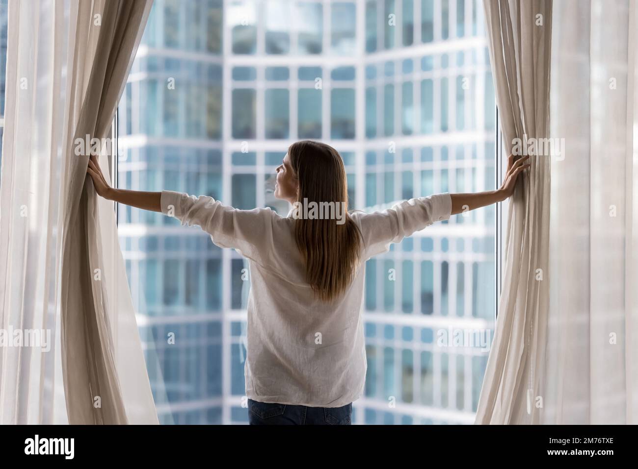 Woman opens curtains looking out window of luxury modern apartment ...