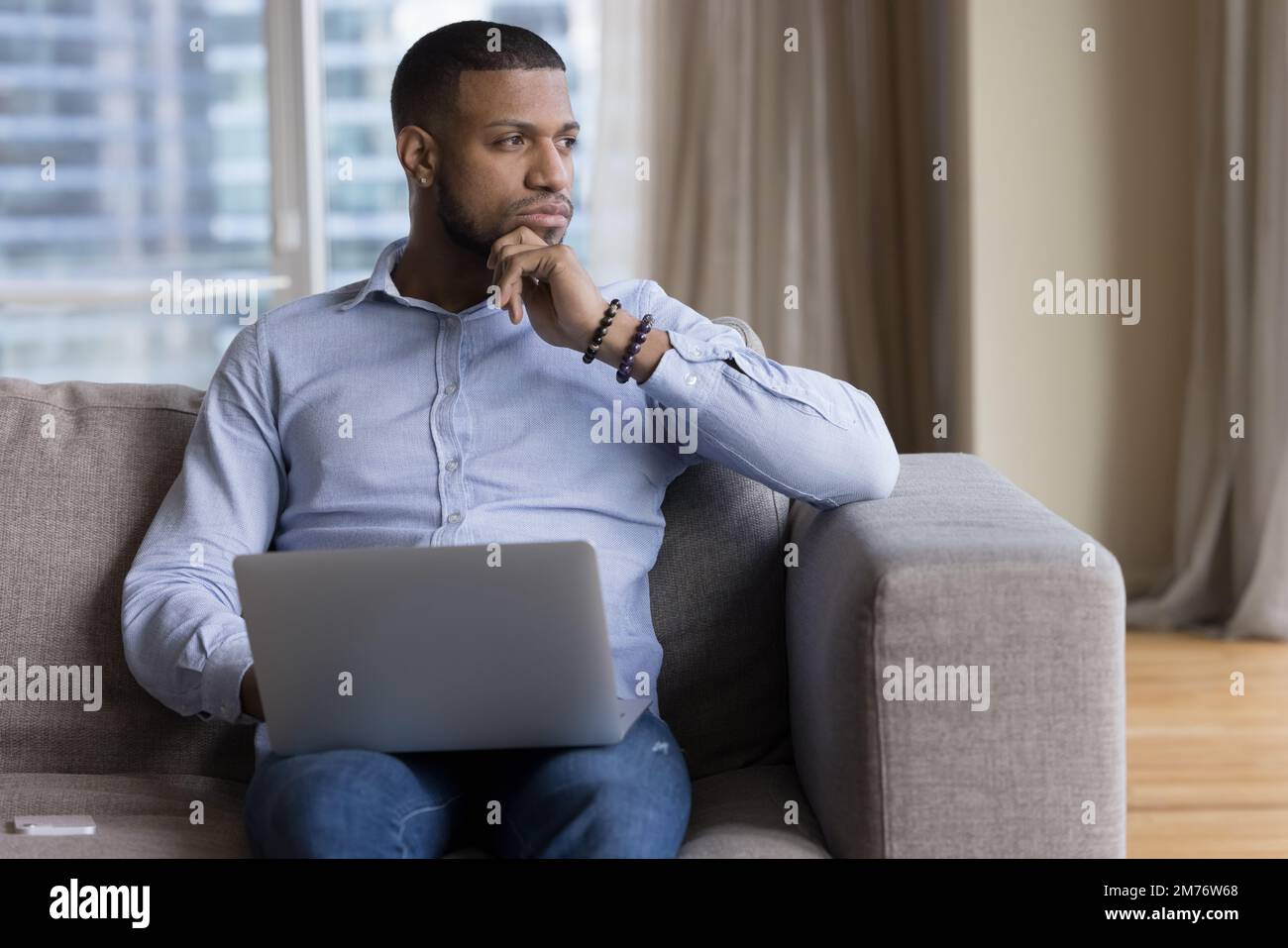 Pensive guy deep in thoughts sitting on sofa with laptop Stock Photo ...