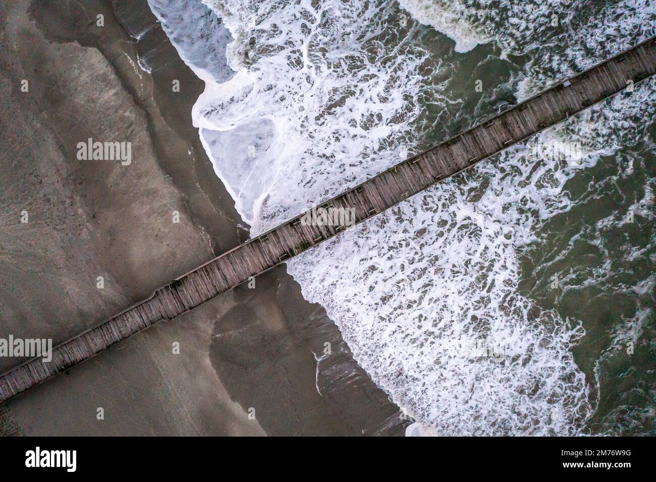 An aerial top view of a wooden pier on sea waves crashing against the ...