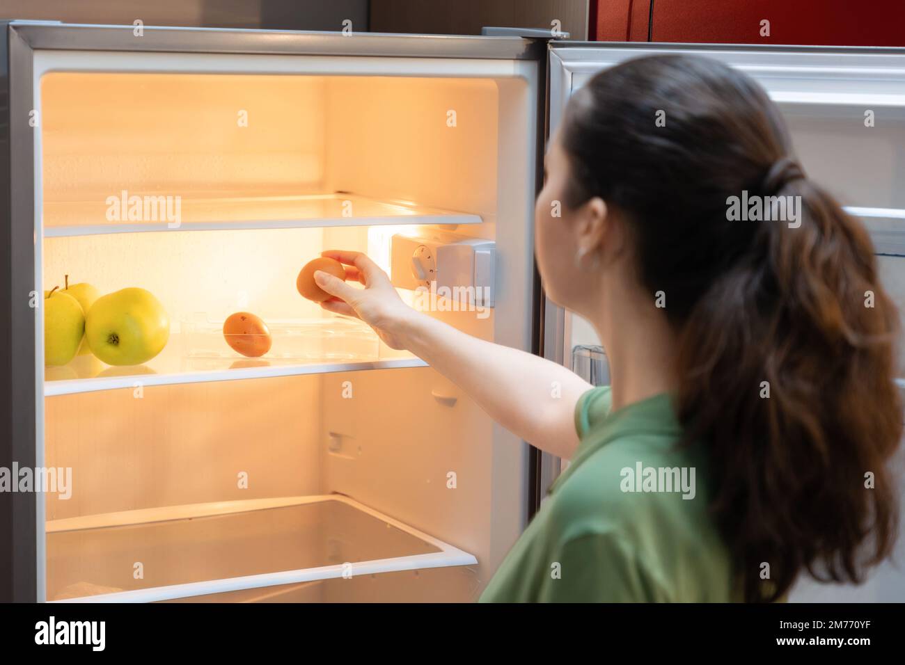 Back view of Caucasian woman takes egg out of empty refrigerator ...
