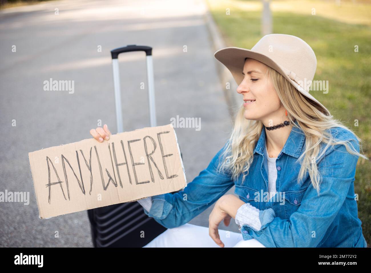 Joyful woman hopefully wait passing car sitting with suitcase and ...