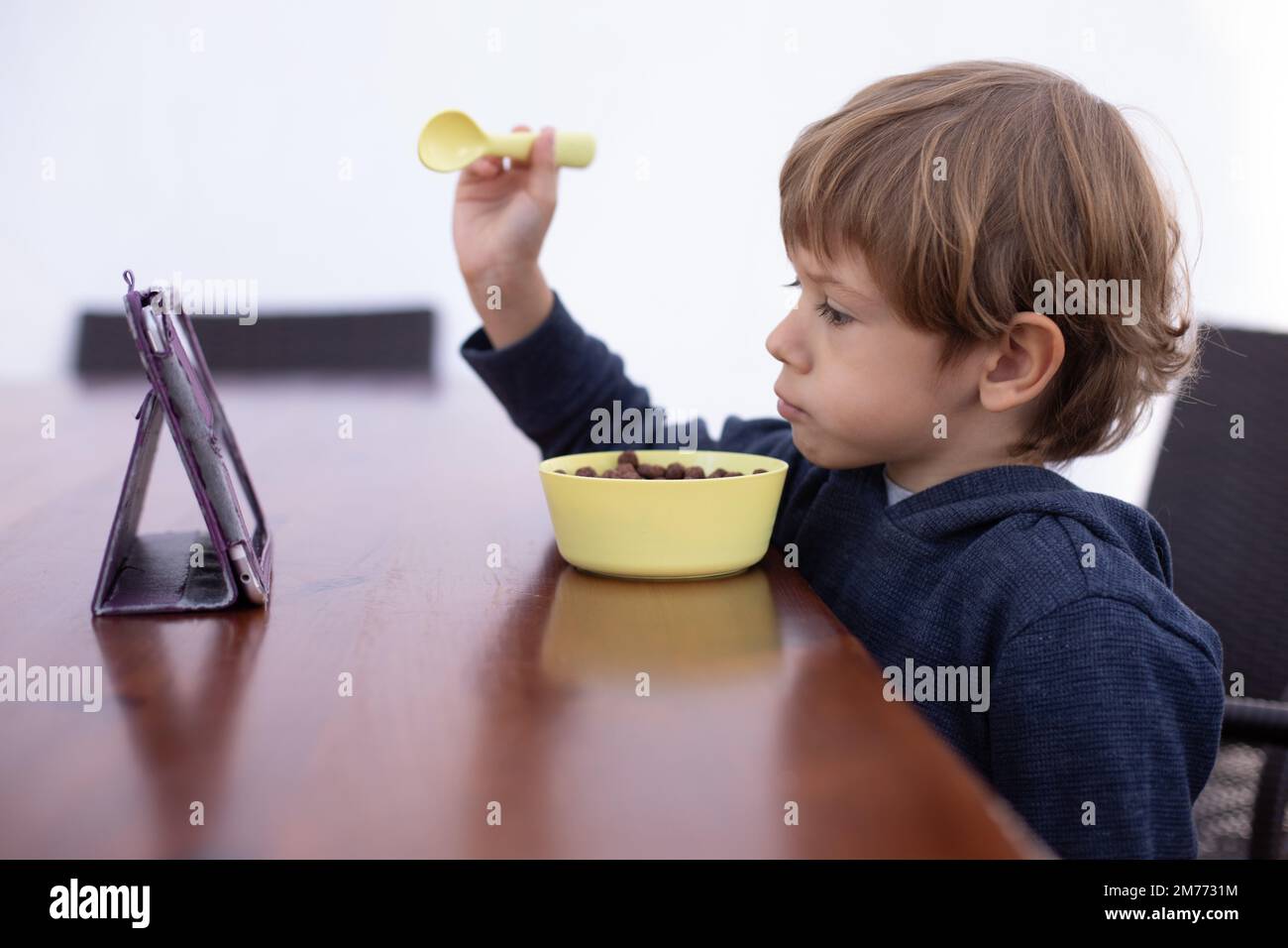 Brown haired boy sit at table and with interest watch cartoon on tablet ...