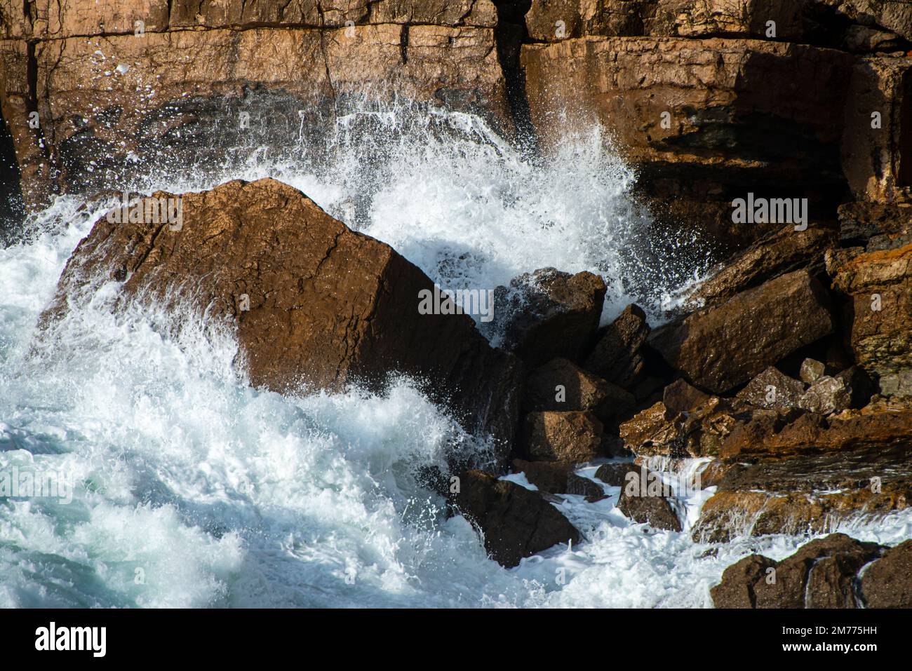 A powerful Atlantic Ocean wave crashes against rugged coastal rocks ...