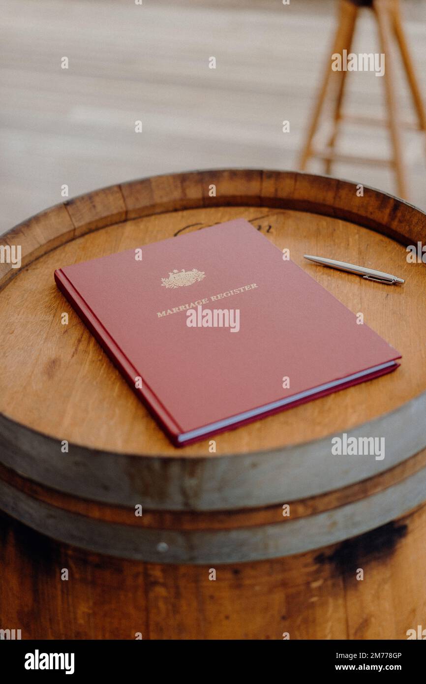A vertical shot of a red marriage register book and a pen on a wooden ...
