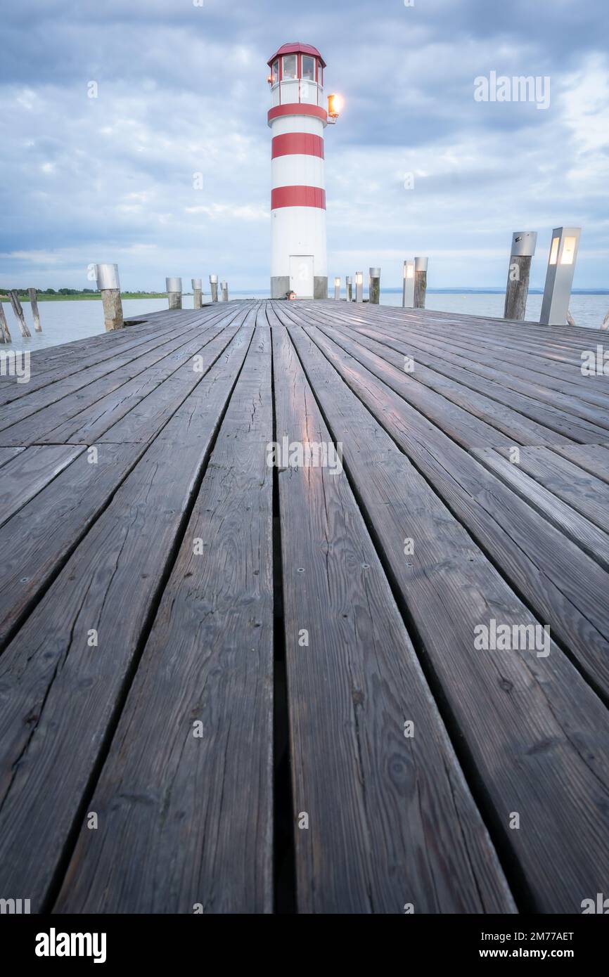 Red and white lighthouse on a cloudy morning with wooden jetty leading ...