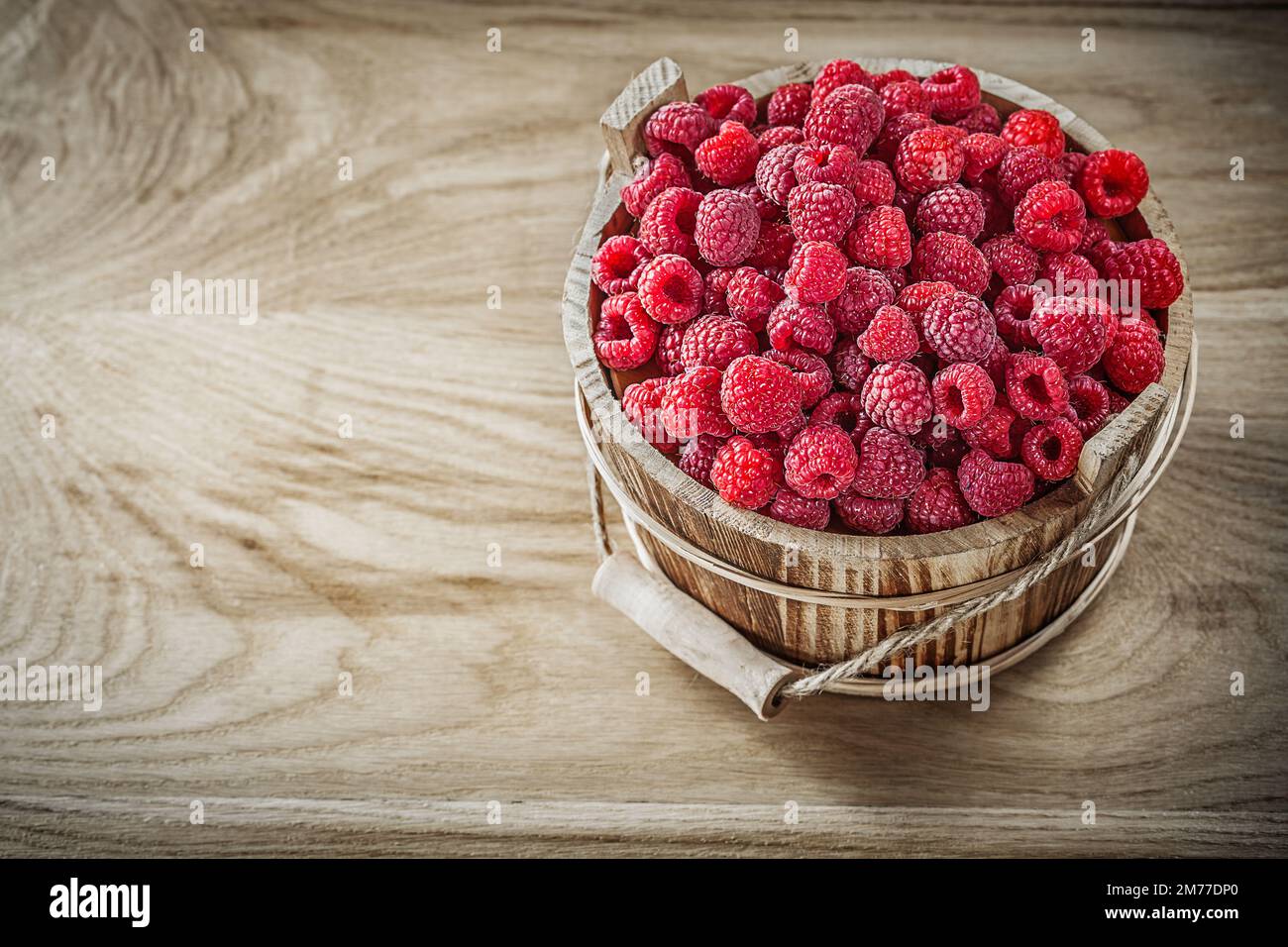 Red juicy raspberries in bucket on wooden board Stock Photo - Alamy