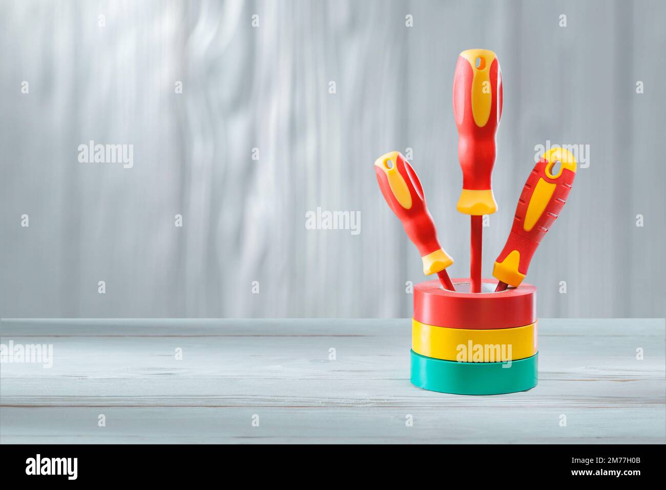 three red yellow insulated electrical screwdrivers standing in stack of rolls insulation tapes ...
