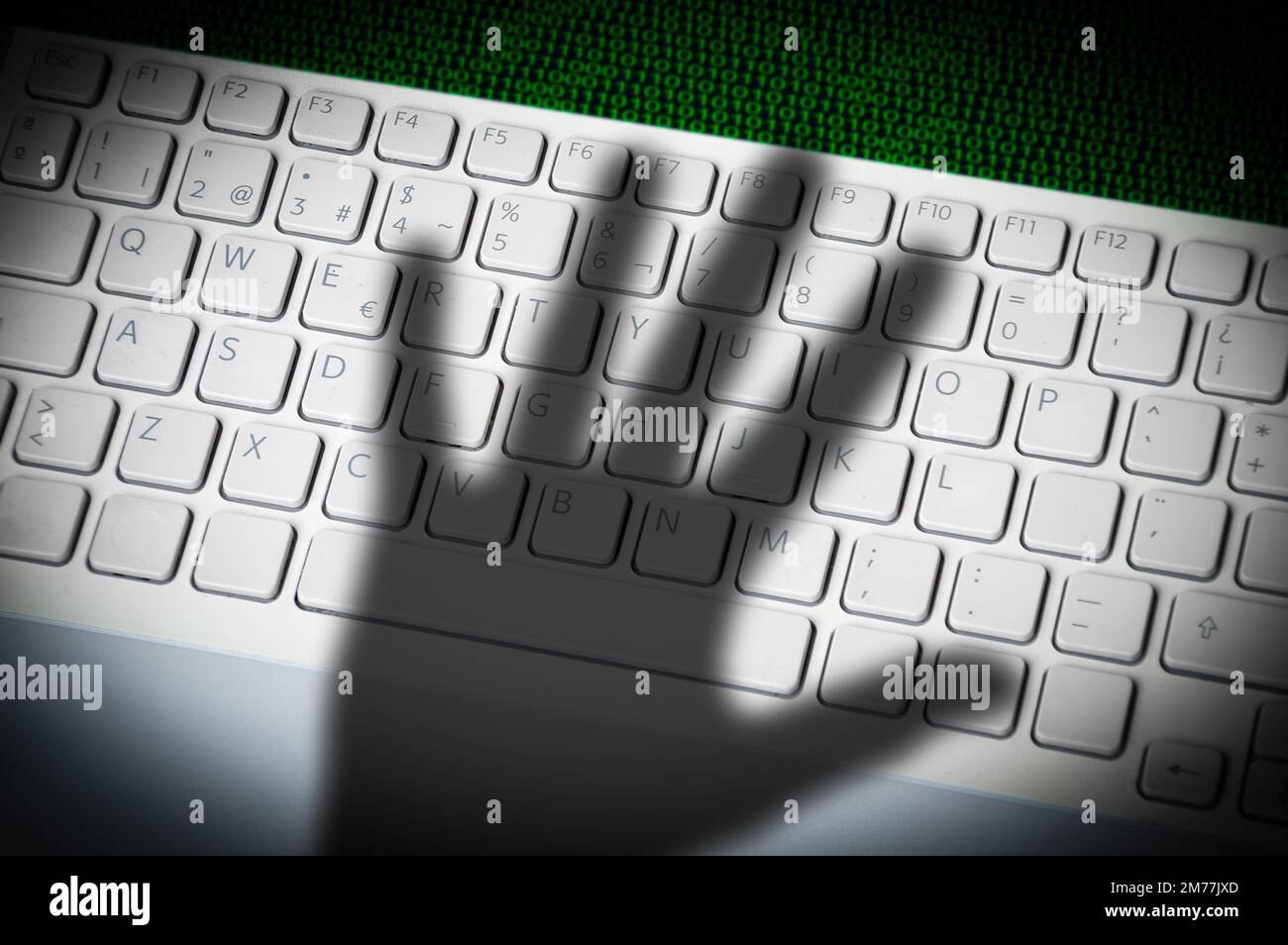 A menacing hand shadow on a computer keyboard in front of printed ...