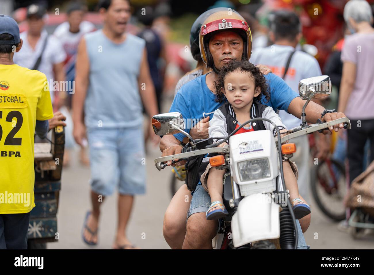 A young child rides on a motorcycle with no helmet. A very common daily ...