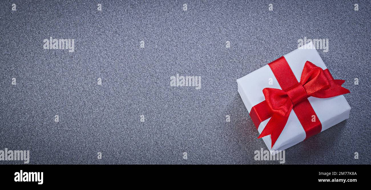 White present box with red tied bow on grey surface copy space holidays ...