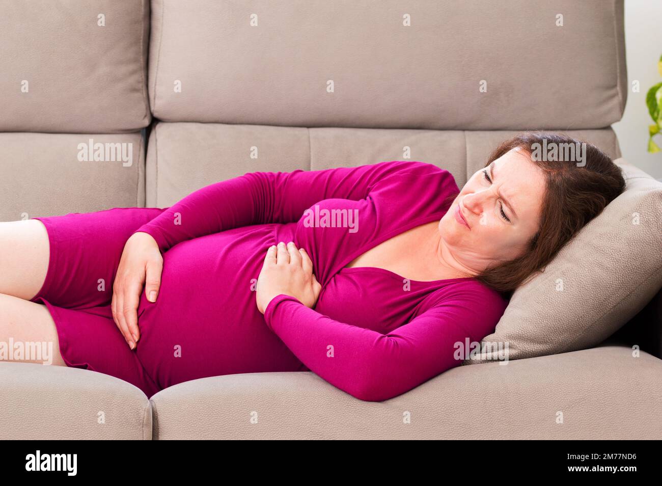 Shot of a pregnant woman suffering belly ache lying on a couch at home ...