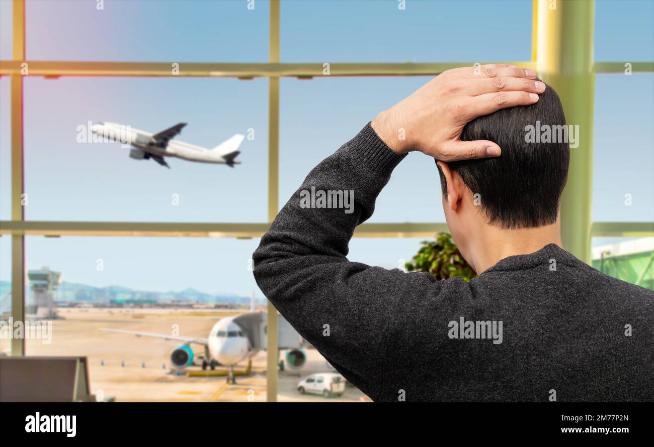 Rear view of a sad man looking at a plane taking off and missing his ...