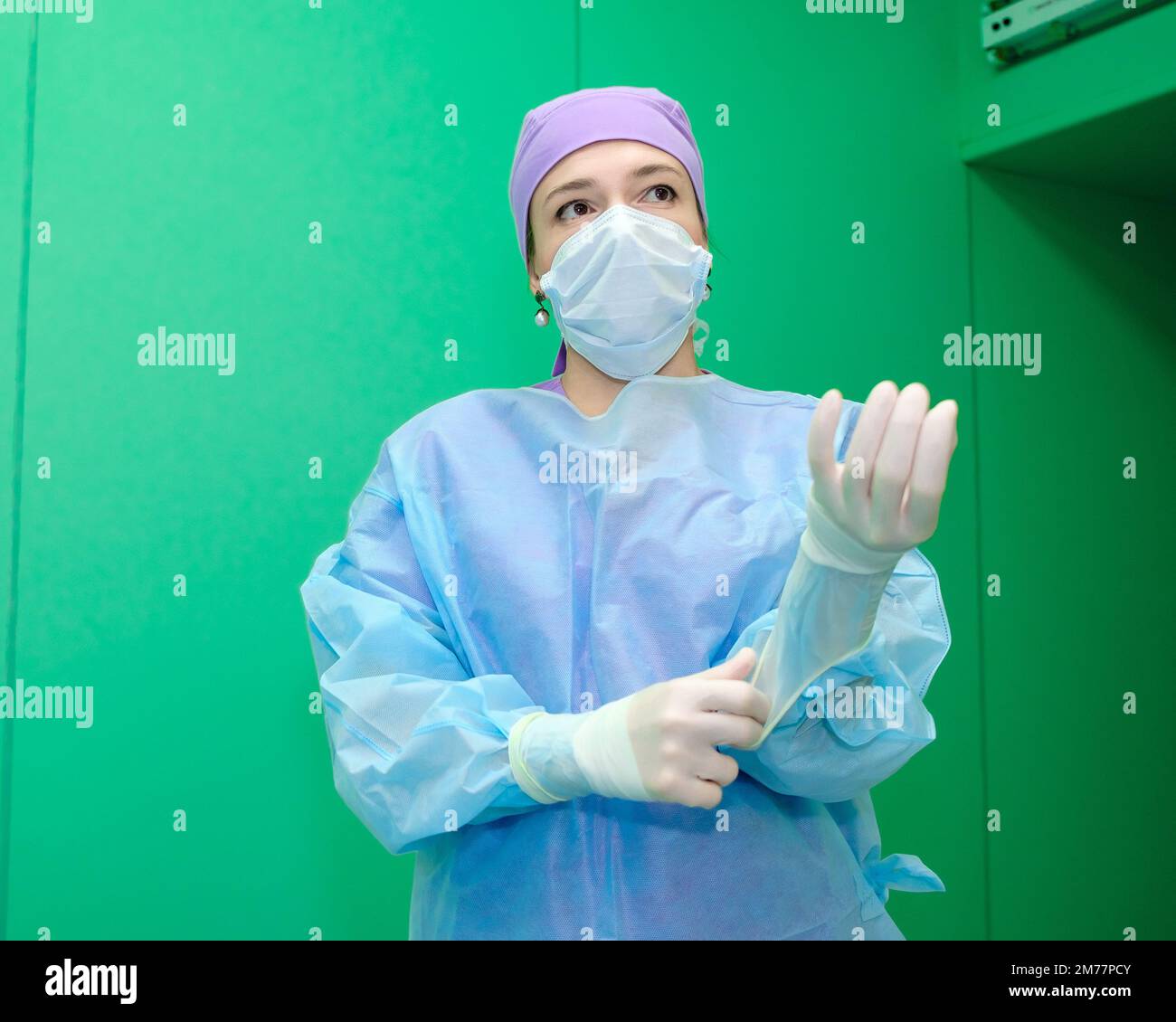 A female doctor in a surgical uniform pulls sterile gloves on her hand ...