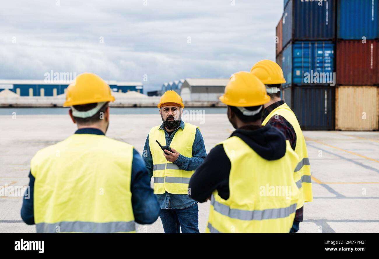 Workers controlling shipping containers at industrial port outdoor ...