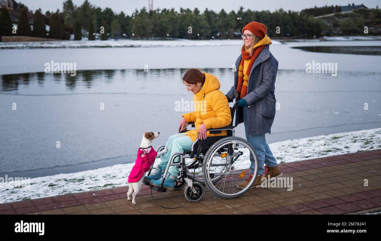 Caucasian woman driving her friend in a wheelchair along the lake in ...