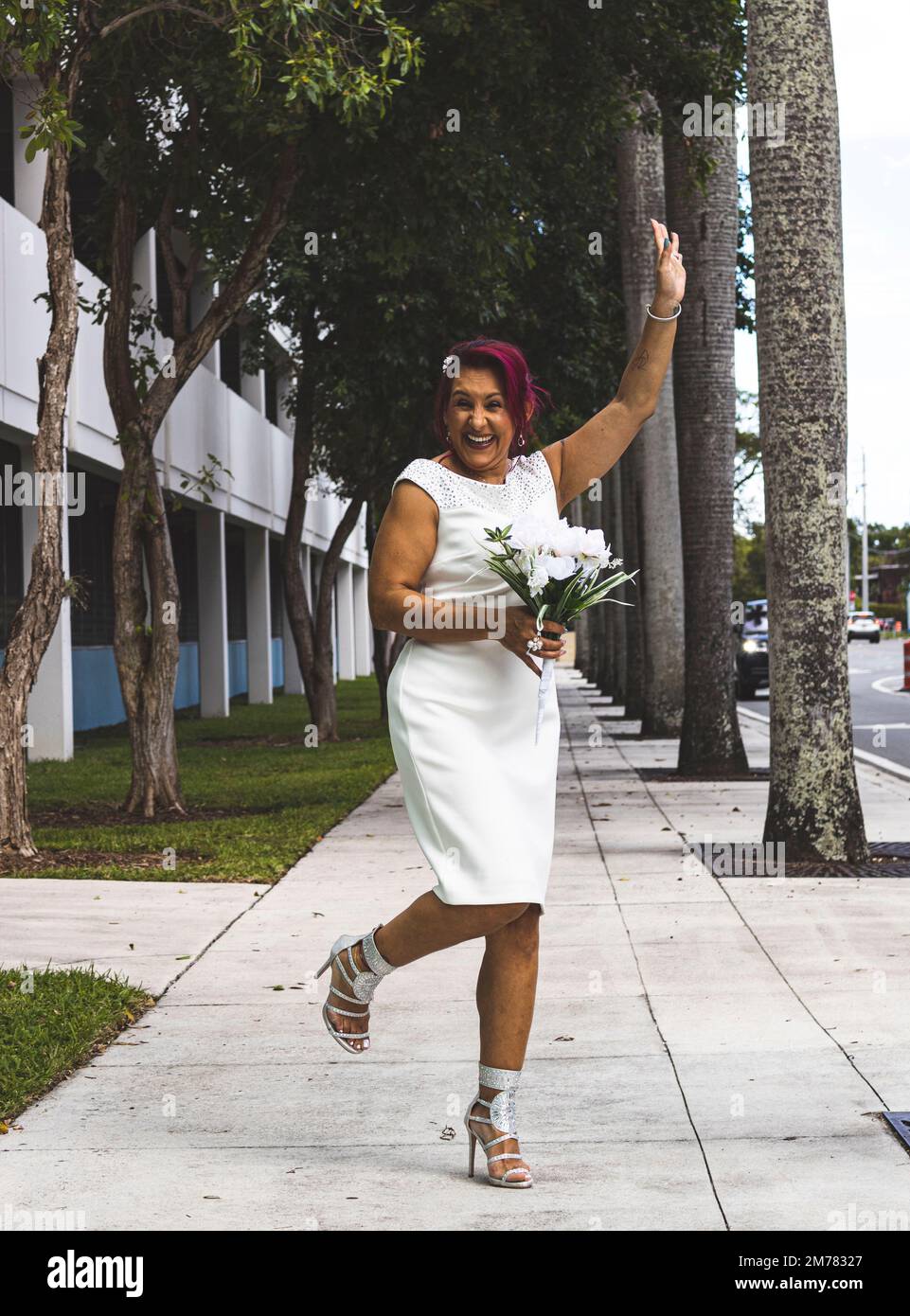 A vertical shot of a happy Hispanic female in a white dress, holding a ...