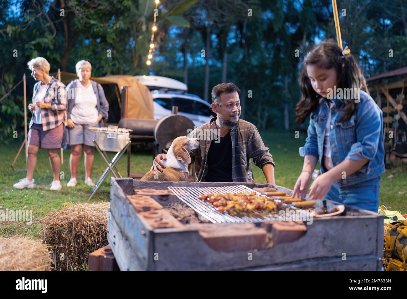 Group of family camper van sitting by fire grilling sausages and ...