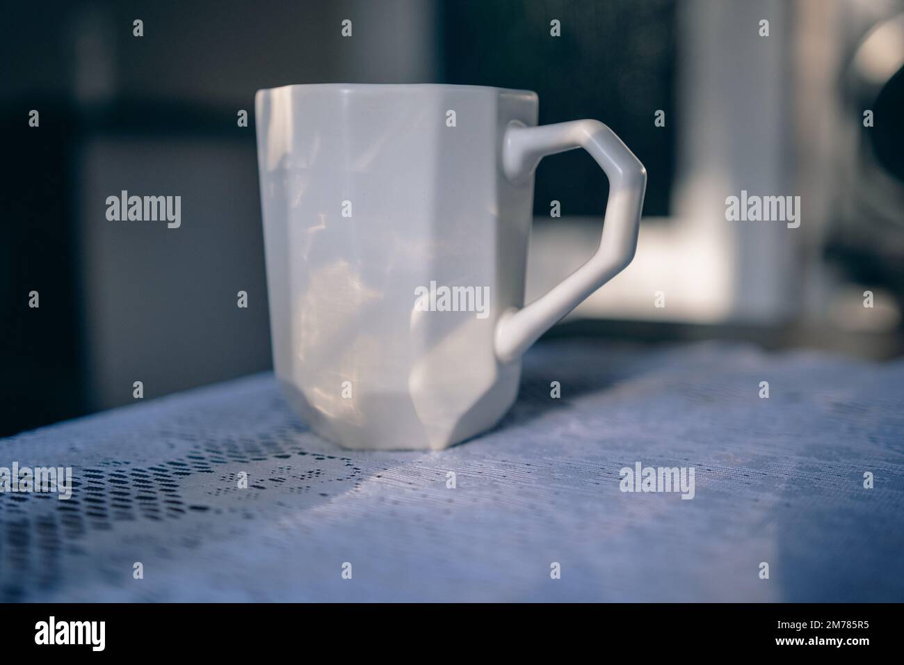 A closeup of a white ceramic mug on a white tablecloth in sunlight ...