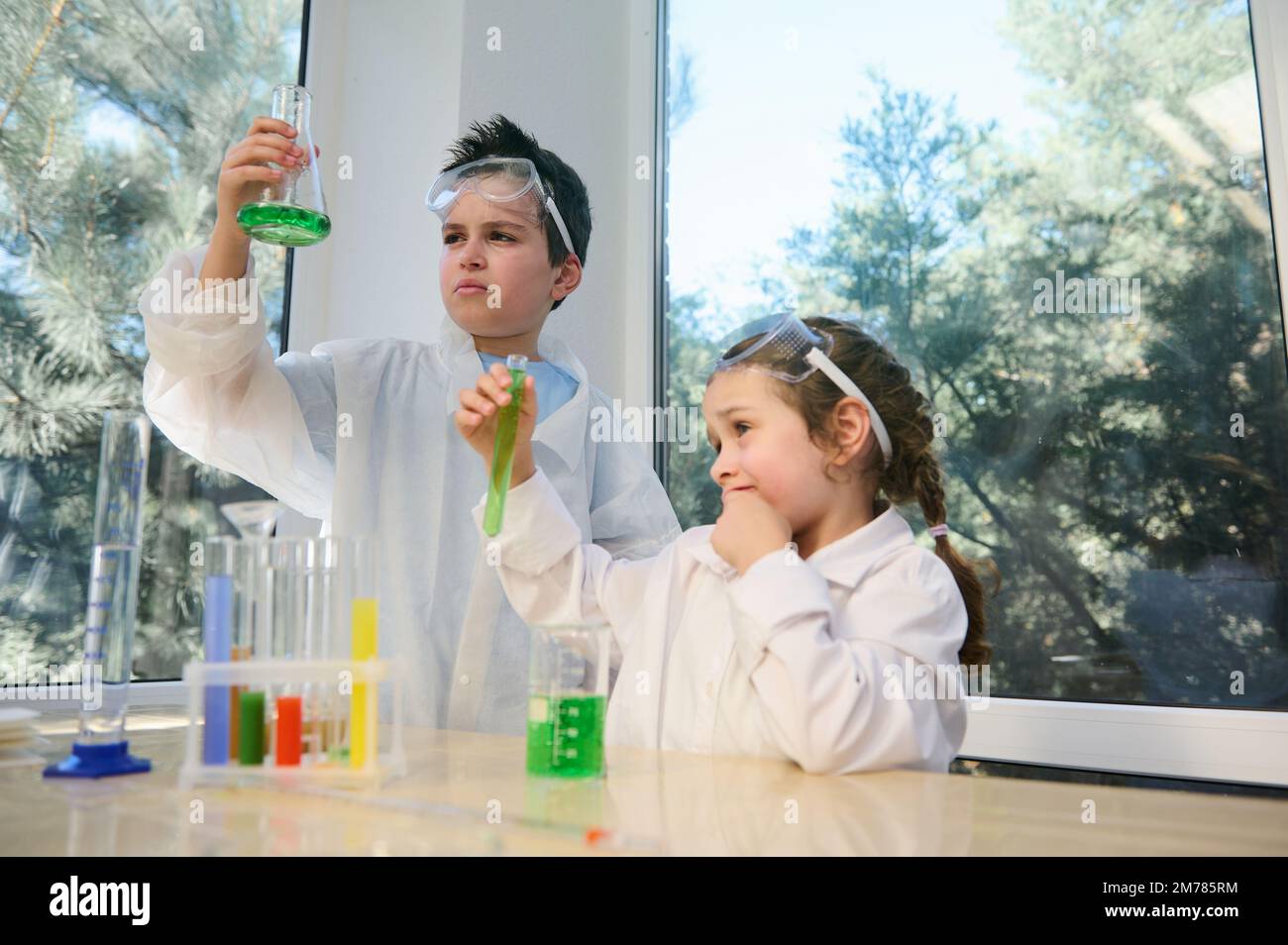 Two smart children, teenage boy and preschooler girl conducting chemical experiments in school ...