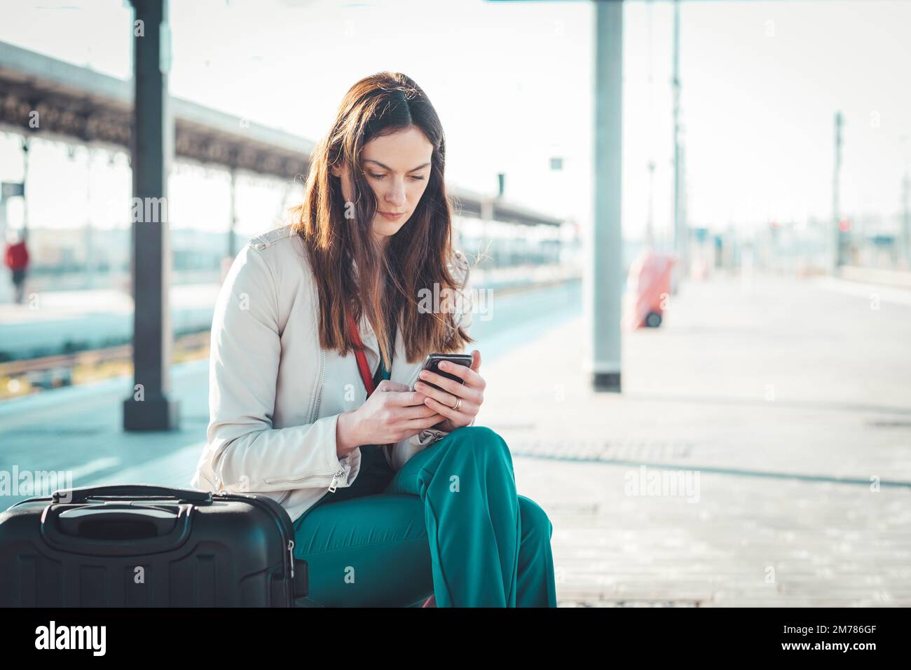 Smiling business woman using smartphone while waiting in a train ...