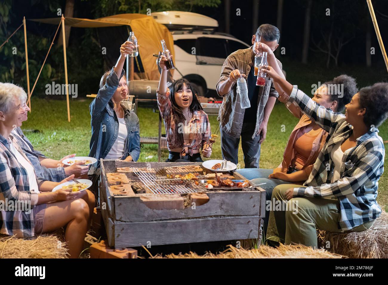 Group of family camper van sitting by fire grilling sausages and ...