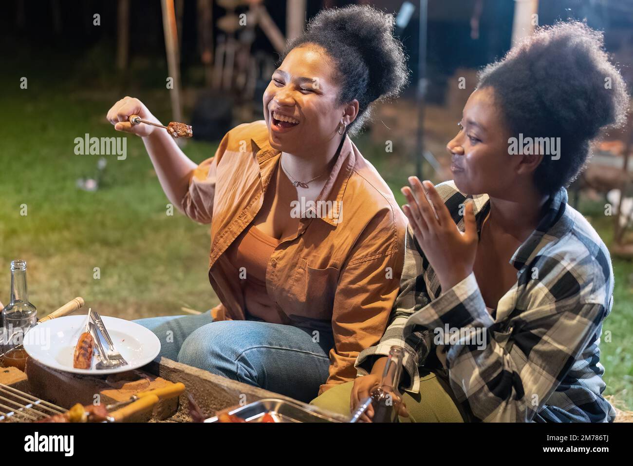 Group of family camper van sitting by fire grilling sausages and ...