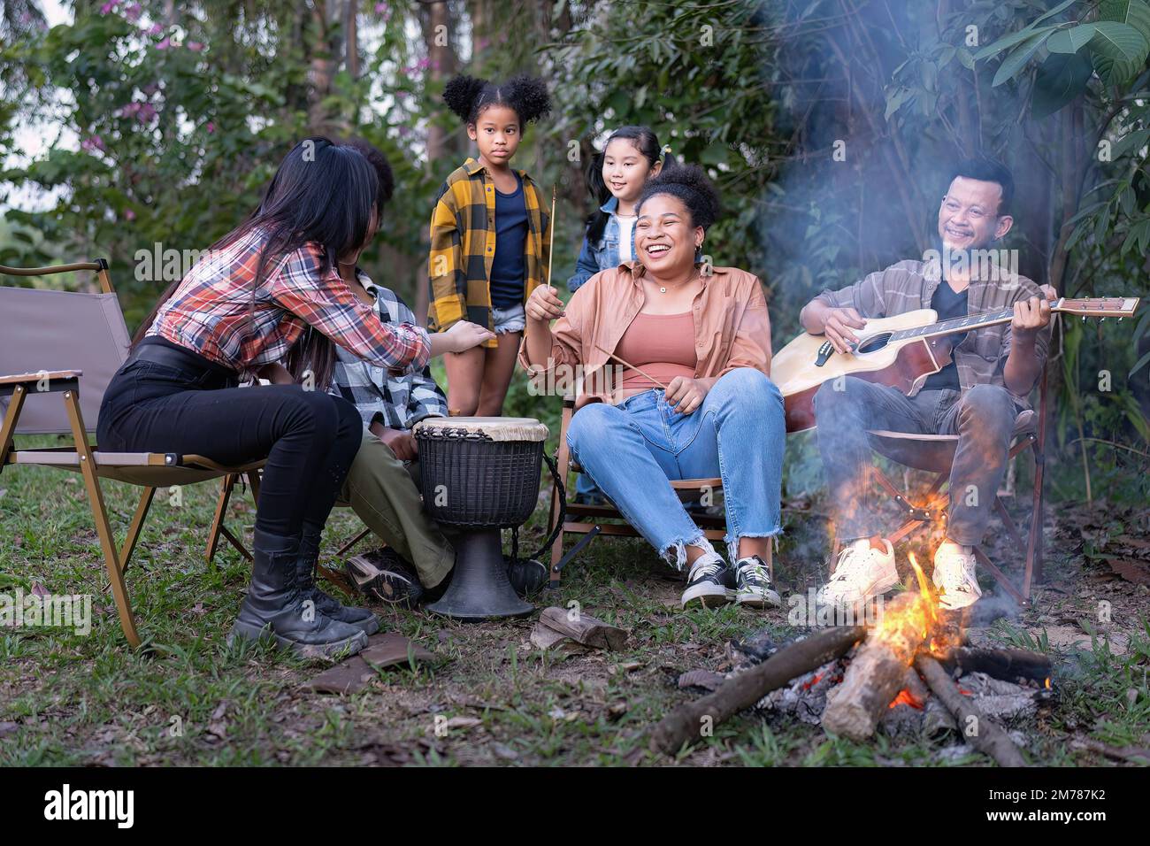 Group of family camper van sitting by fire grilling sausages and ...