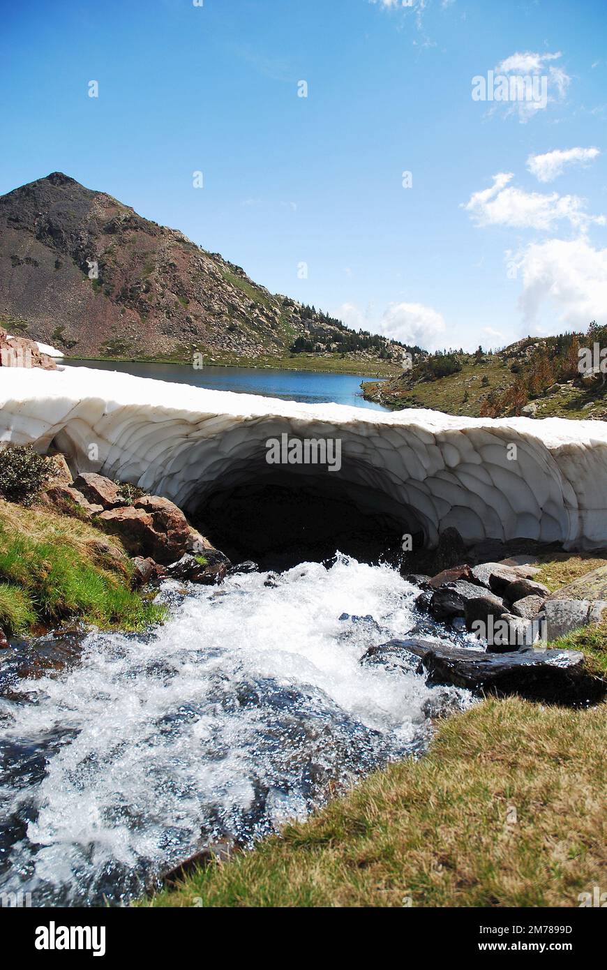 A river flowing under an ice arch with a background of a lake between ...