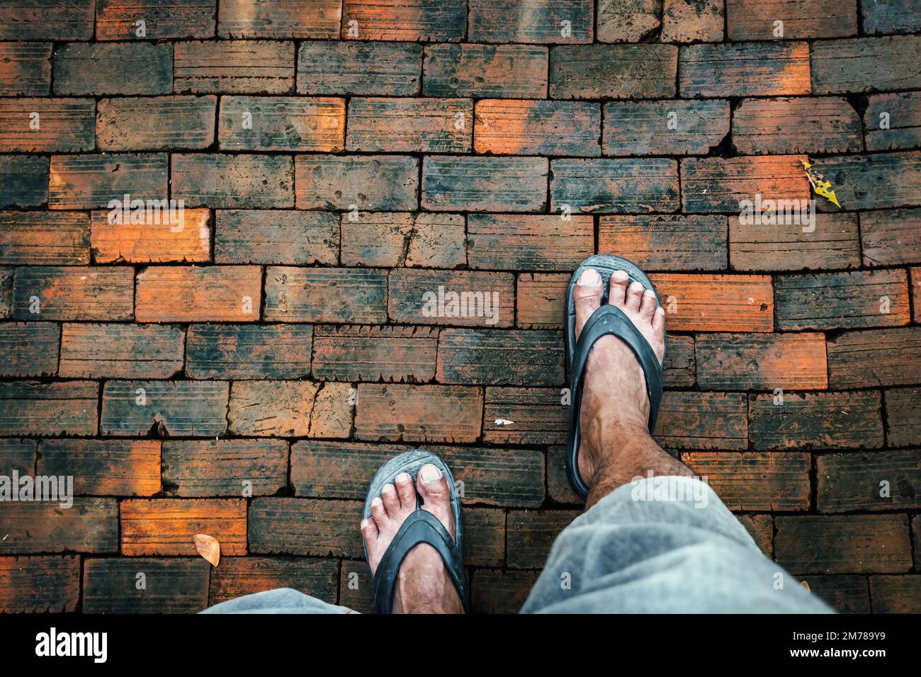 Feet of man wear sandals on old bricks paving stones footpath pattern ...