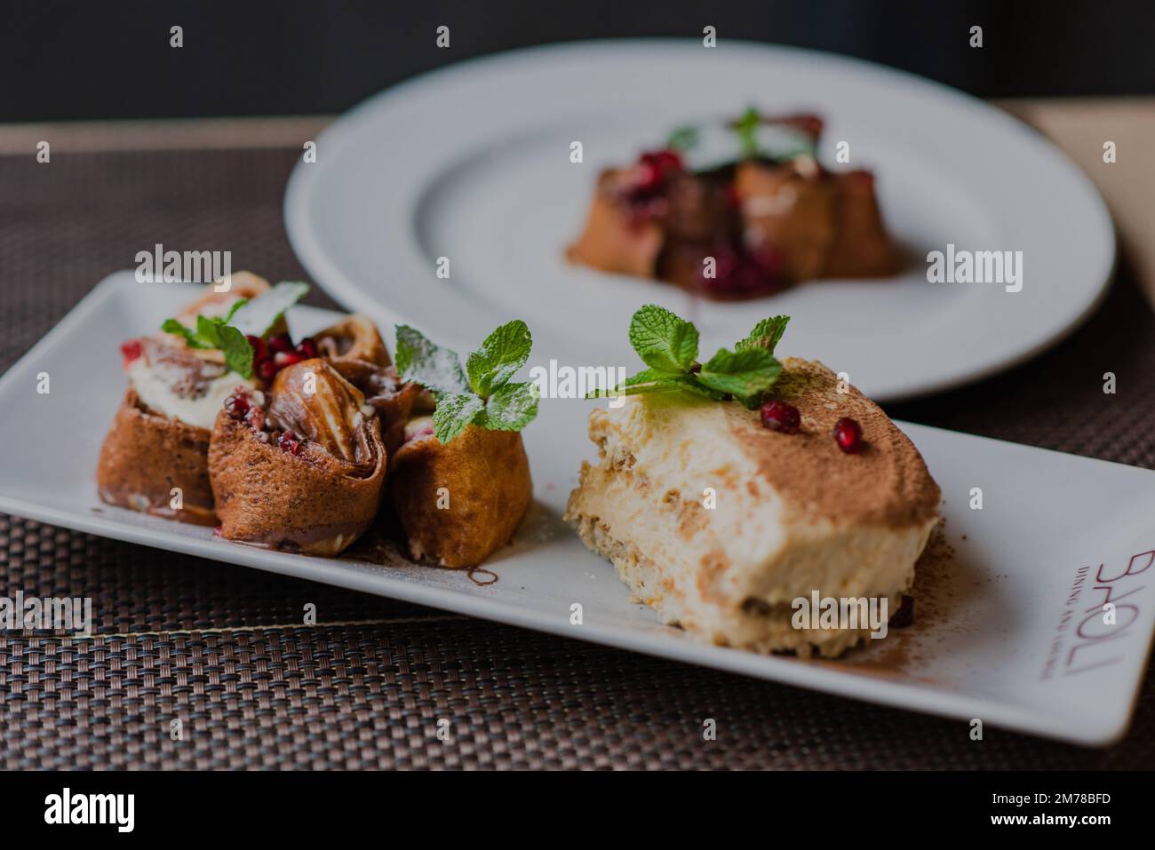 Two deserts on white plates on a table against dark, blurred background ...